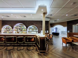 Espaço de bar com parede de tijolos, banquetas e balcão exibindo garrafas.