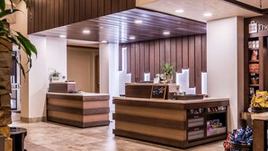 Uma área de recepção de hotel com dois balcões de madeira, uma planta e uma prateleira com lanches.