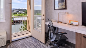 Um espaço de escritório moderno com uma mesa, cadeira e vista para uma varanda com paisagem urbana e montanhas ao fundo.
