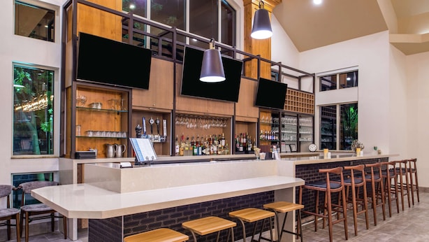 Uma área de bar com balcão, banquetas e diversos tipos de garrafas e copos.