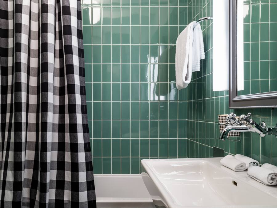 Um banheiro com cortina de chuveiro quadriculada, pia branca com espelho e paredes revestidas de azulejos verdes.
