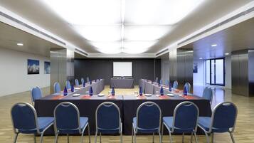 Uma sala de conferências com uma mesa comprida, cadeiras azuis e uma tela de projetor.