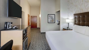 Quarto de hotel com uma cama, escrivaninha com televisão de tela plana, cafeteira e quadro na parede.