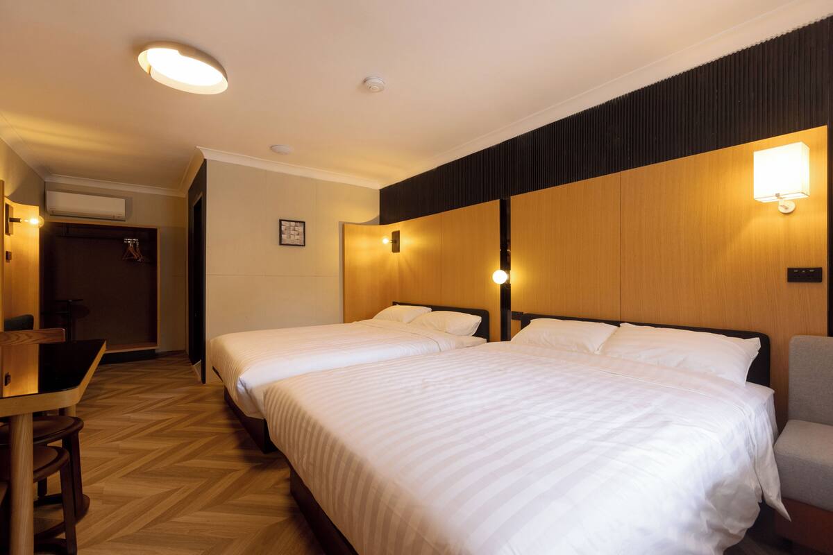 Quarto de hotel com duas camas, uma escrivaninha e uma cadeira.