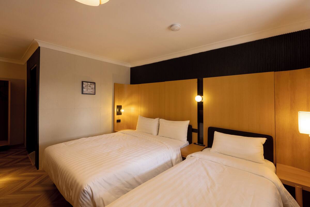 Quarto de hotel com duas camas de solteiro, cabeceiras de madeira e luminárias de cabeceira.