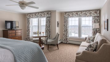 Quarto de hotel com cama, escrivaninha com cadeira, televisão e sofá.