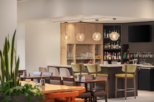 Uma área de bar moderna com prateleiras de madeira, luminárias pendentes e uma televisão de tela plana.