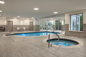 Uma grande piscina interior com hidromassagem, paredes revestidas de azulejos e uma porta para um vestiário.