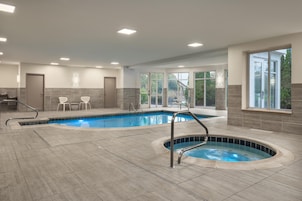 Uma área interna de piscina moderna com hidromassagem, espaço para relaxar e grandes janelas.