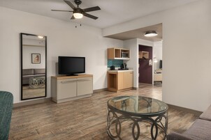 Uma sala de estar moderna com televisão de tela plana, uma mesa de centro de vidro e um ventilador de teto.