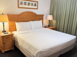 Quarto de hotel com uma cama grande, duas mesas de cabeceira, um abajur, um relógio e um quadro na parede.