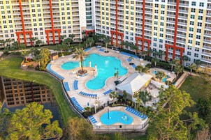 Um hotel com várias piscinas, um jardim bem cuidado e um edifício grande com varandas.