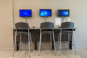 Uma área de recepção com três monitores de computador em uma parede, um balcão de atendimento e duas cadeiras altas.
