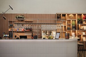 Uma área de bar com balcão, prateleiras com garrafas, copos e um quadro de cardápio.