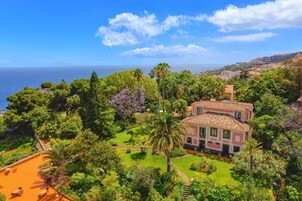 Um imóvel costeiro com uma casa grande rodeada por vegetação exuberante e vista para o mar.