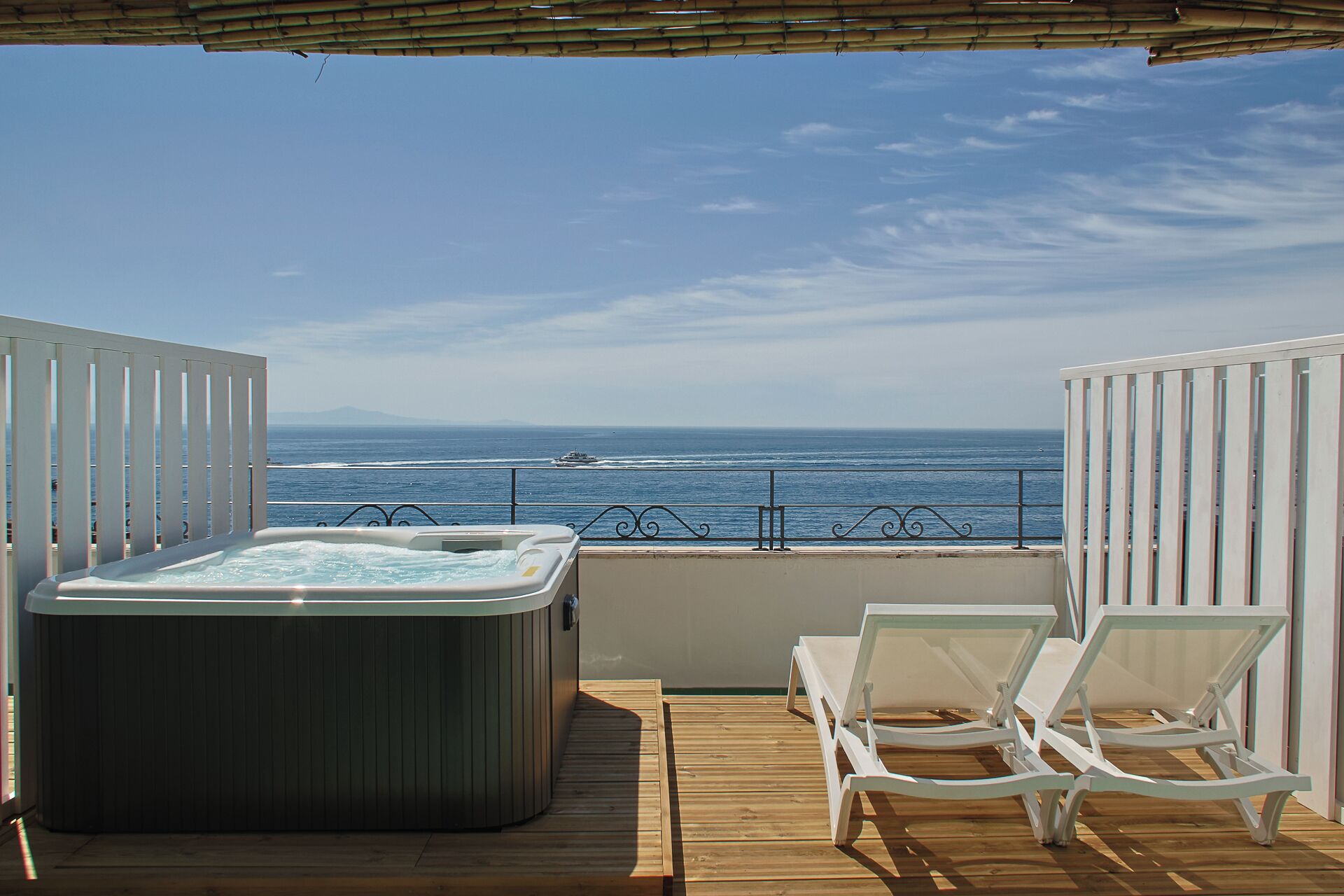 Uma banheira de hidromassagem numa varanda de madeira com vista para o oceano e cadeiras.