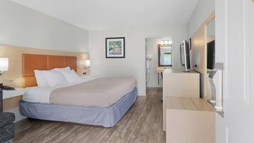 Quarto de hotel com cama, mesa de cabeceira, luminária e escrivaninha com cadeira.