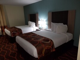 Quarto de hotel com duas camas, mesa de cabeceira, abajur e carpete estampado.