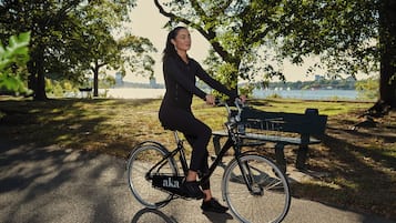 Uma pessoa andando de bicicleta num parque, com um banco e árvores ao fundo.