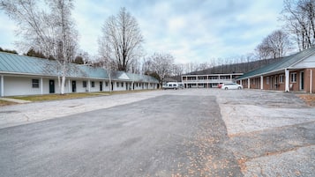 Um motel com área de estacionamento central e vários quartos com telhados verdes.