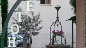 Uma entrada murada com um arco decorativo, uma pequena fonte e um edifício ao fundo.