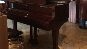 Um piano de cauda numa sala com painéis de madeira, um vaso com flores cor-de-rosa e corações decorativos pendurados.