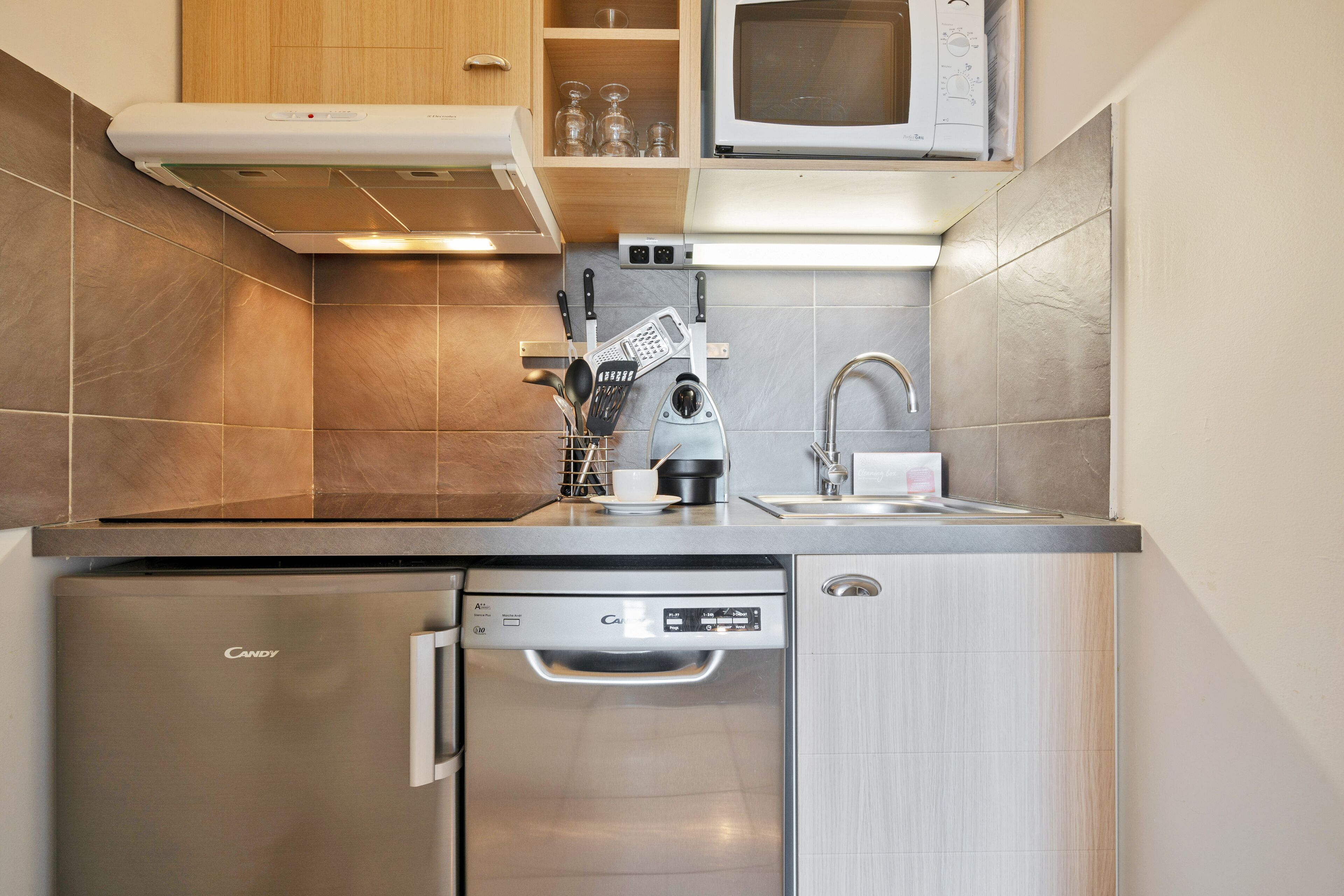 Cozinha compacta equipada com micro-ondas integrado, frigorífico em aço inoxidável e máquina de lavar louça.