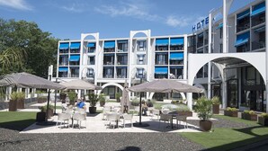 Um hotel com várias varandas, áreas de estar ao ar livre com guarda-sóis e um jardim bem cuidado.