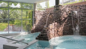 Piscina com cascata, cercada por paredes de pedra e amplas janelas.