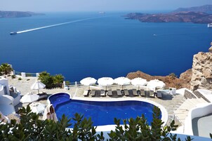 Área de piscina com espreguiçadeiras e guarda-sóis com vista para uma grande extensão de água.