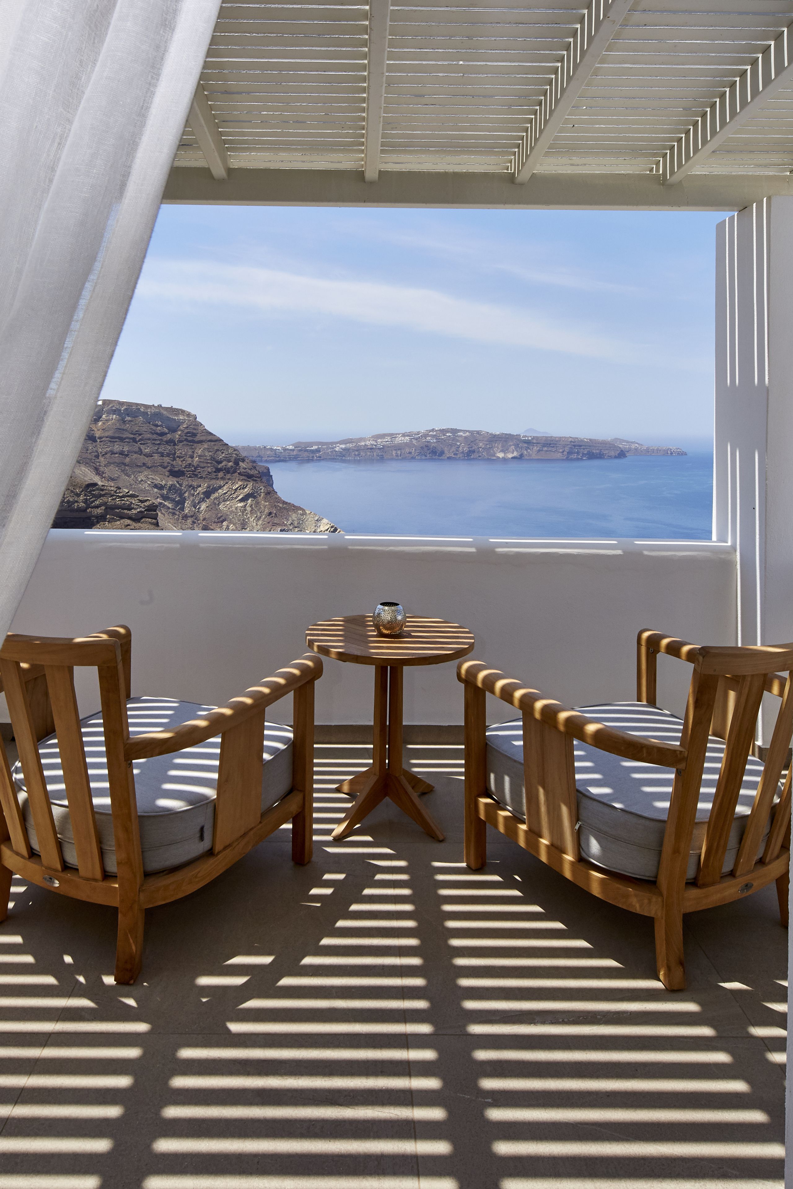 Varanda com cadeiras de madeira e uma pequena mesa, com vista para a paisagem costeira com falésias e o mar.
