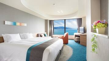 Quarto de hotel moderno com uma cama grande, uma escrivaninha, uma cadeira e vista para o mar.