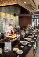 Buffet montado com várias estações de comida, um chef a preparar refeições e um painel de ementa.