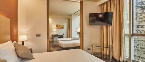 Quarto de hotel com uma cama grande, uma escrivaninha, uma cadeira, uma televisão e uma janela com cortinas.
