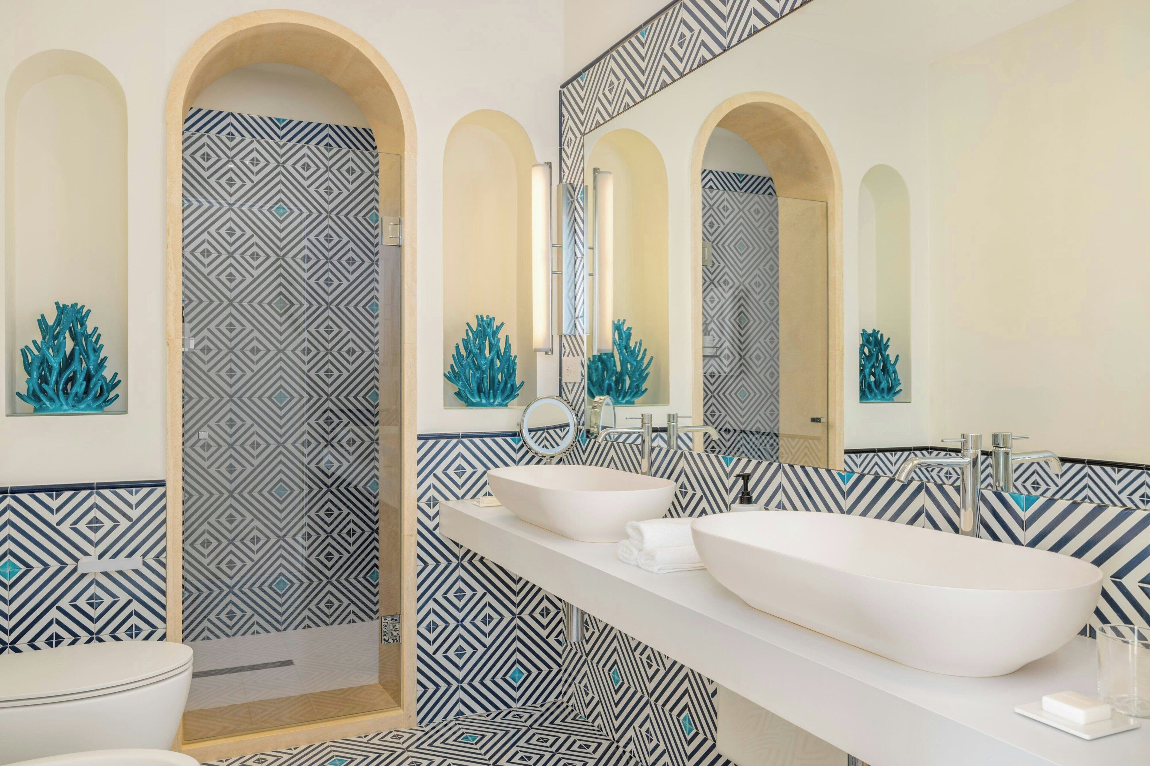 Banheiro com duas pias, um espelho e esculturas de coral decorativas.