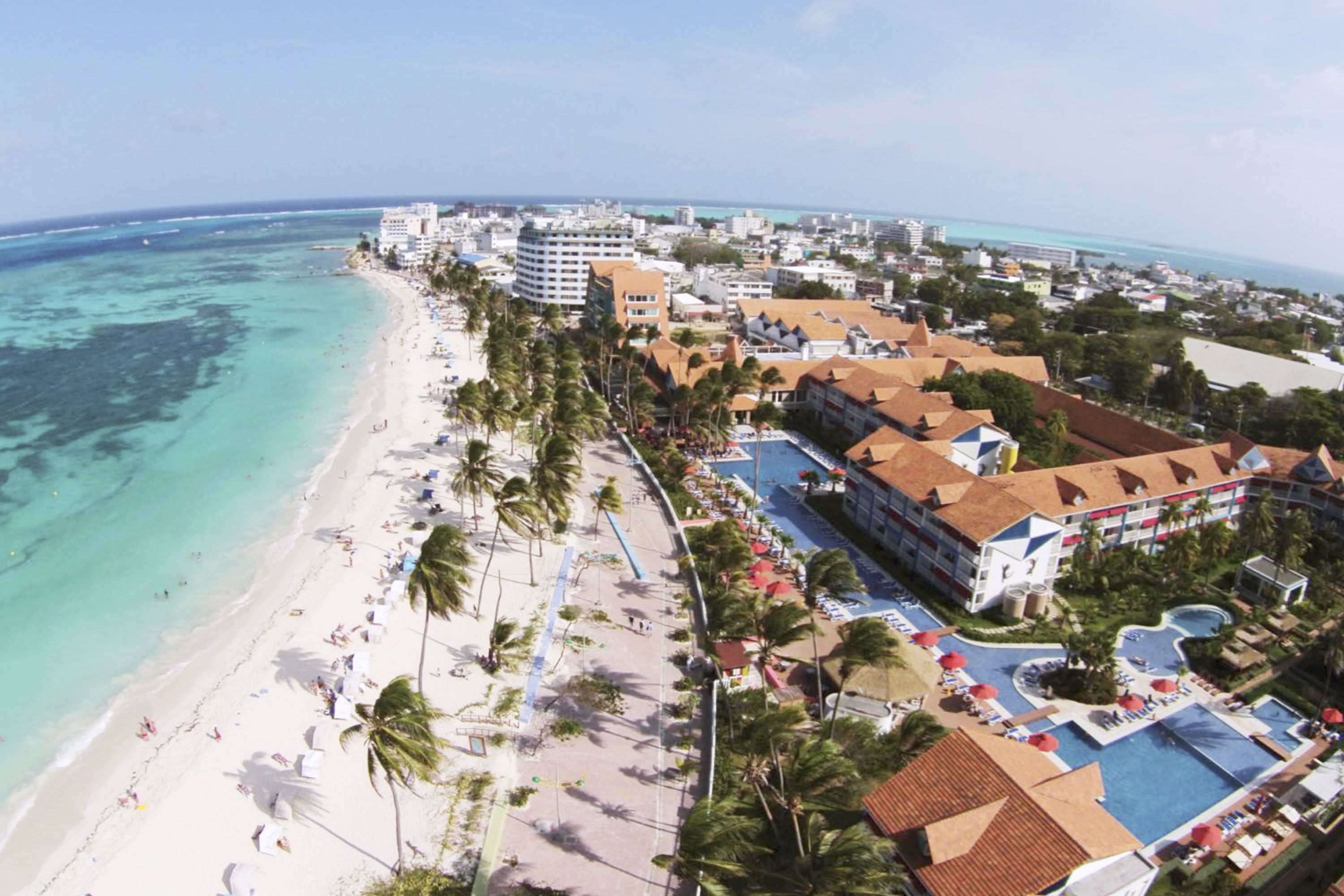 Uma estância costeira com praia, área de piscina e vários edifícios.