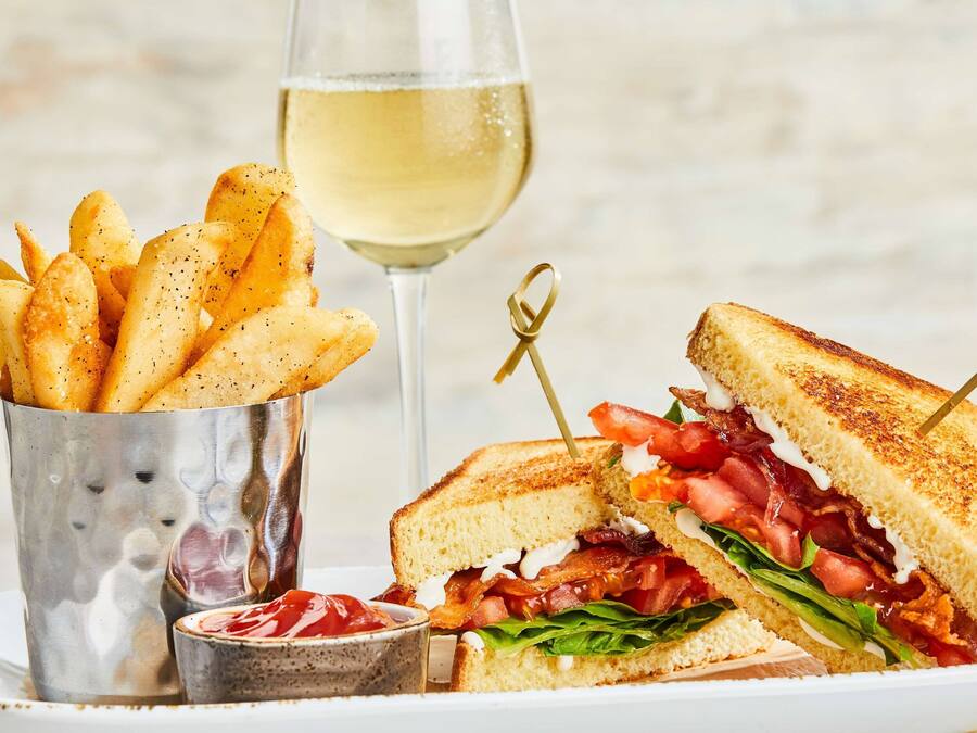 Um sanduíche acompanhado de batatas fritas e um copo de vinho branco.