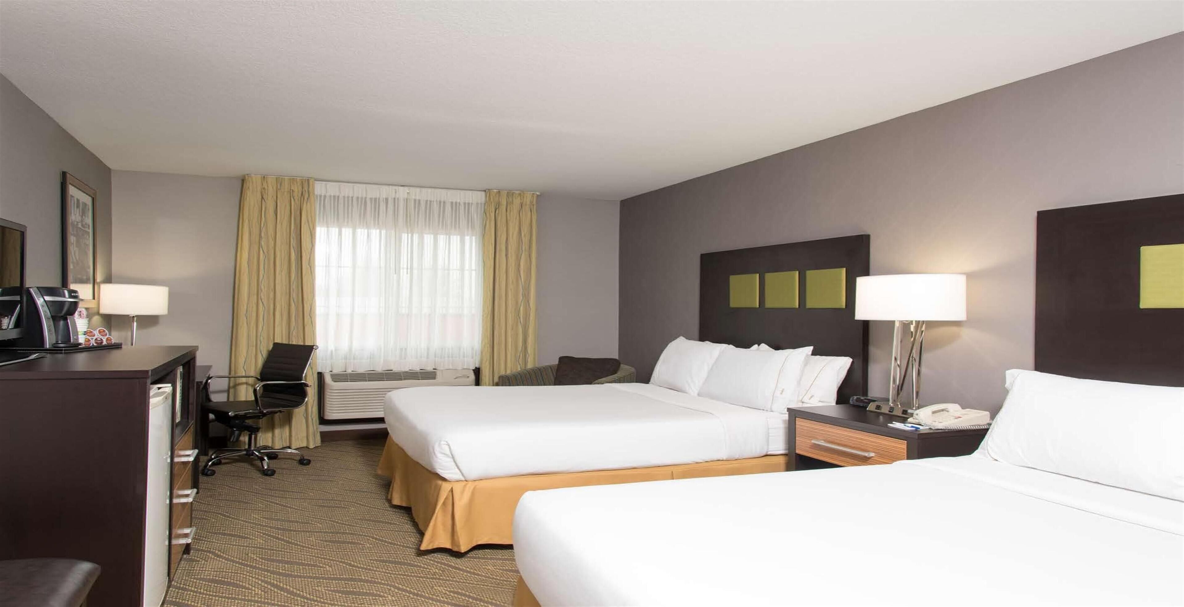 Quarto de hotel com duas camas, uma escrivaninha com computador, uma cadeira, um abajur e um telefone.