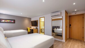 Quarto de hotel com duas camas, uma escrivaninha, televisão e ar condicionado.