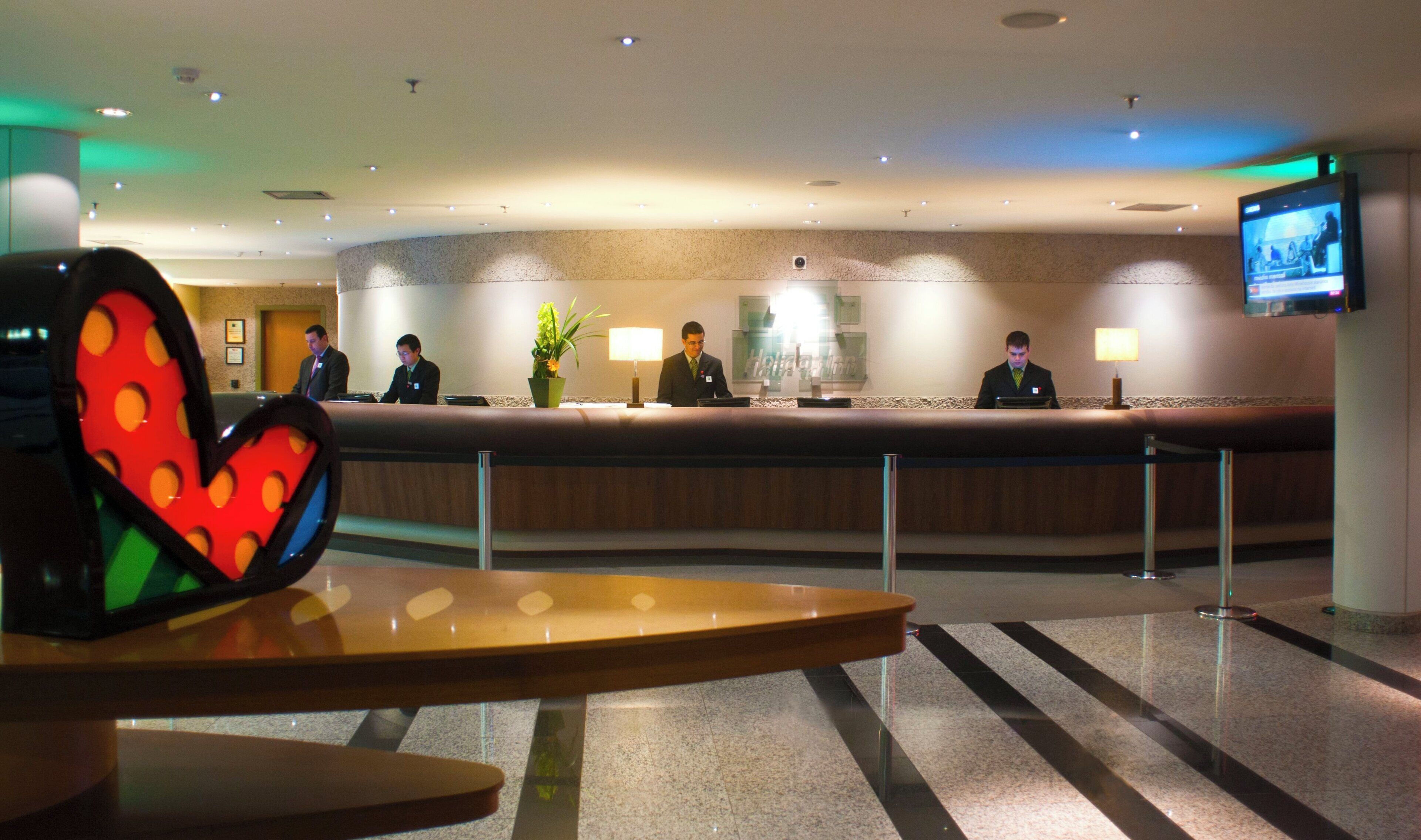 Uma receção de hotel com design curvo, várias lâmpadas e uma tela de televisão.