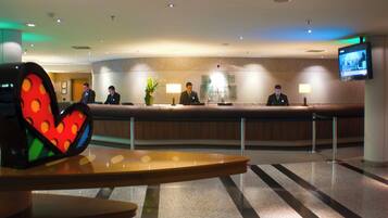 Uma receção de hotel com design curvo, várias lâmpadas e uma tela de televisão.