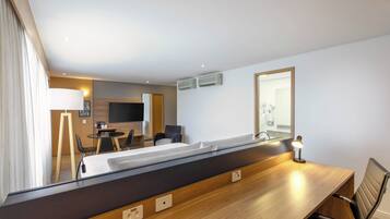 Quarto de hotel moderno com uma mesa de madeira comprida, um espelho grande e uma televisão de tela plana.