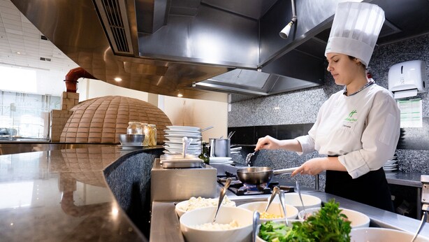 Um chef preparando comida em uma cozinha moderna com eletrodomésticos de aço inoxidável e um forno de tijolos.