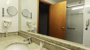 Uma casa de banho com uma pia, dois espelhos, um secador de cabelo e um chuveiro.