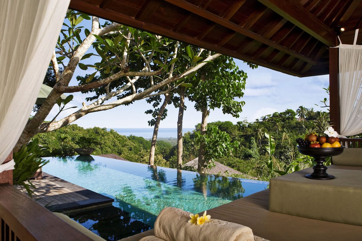 Uma piscina infinita com vista para o oceano, rodeada por vegetação exuberante e uma pérgula de madeira.