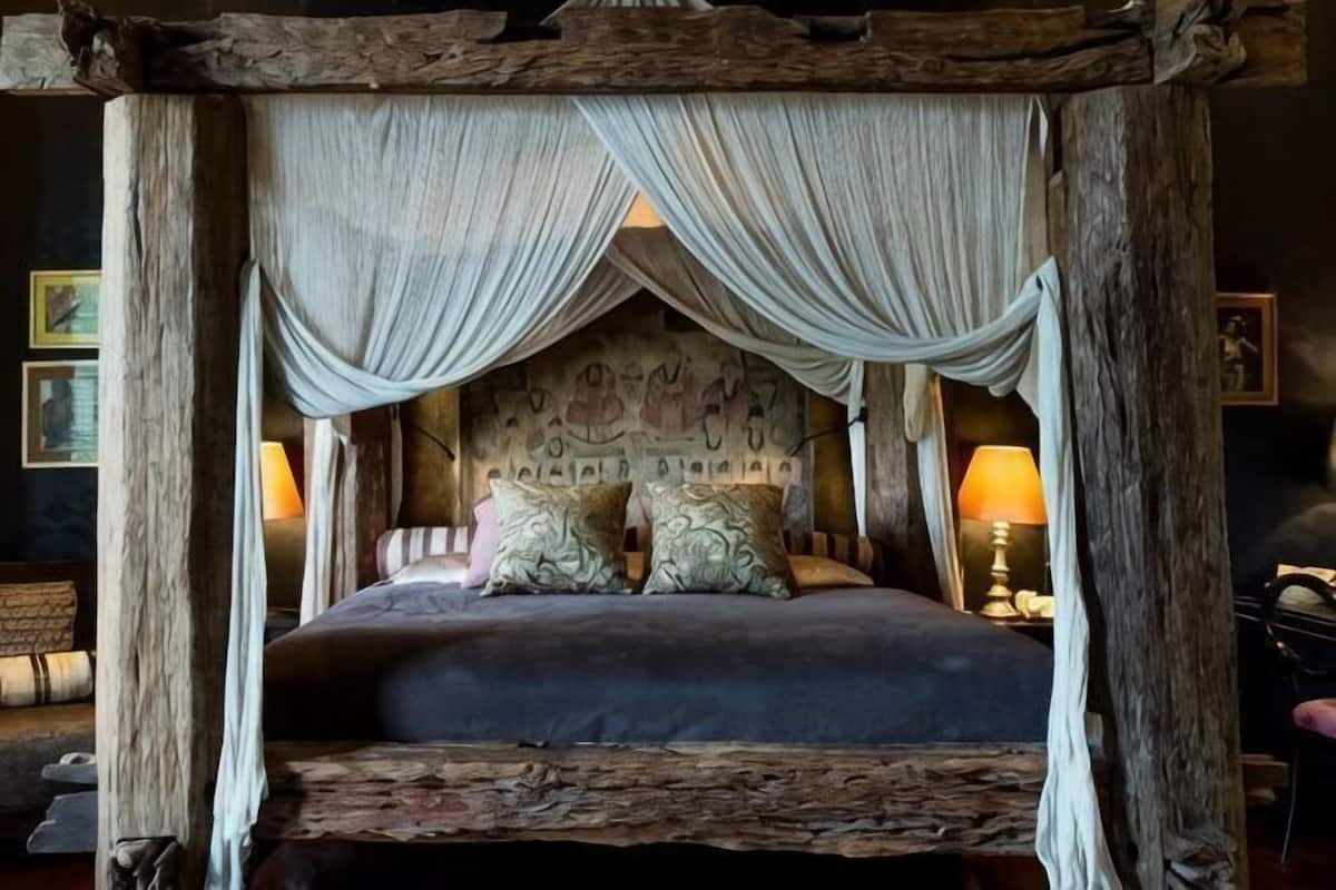 Uma cama de dossel com cortina, cabeceira com padrão floral e duas luminárias de cabeceira.