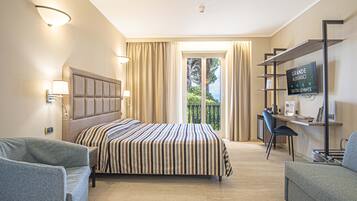 Quarto de hotel com cama, escrivaninha, cadeira e televisão.