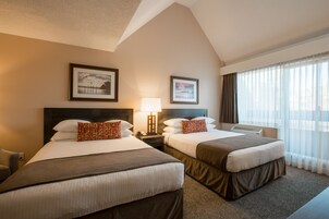 Quarto de hotel com duas camas, uma mesa de cabeceira com abajur e uma janela com cortinas.