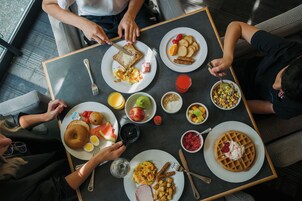 Um grupo de pessoas sentado em volta de uma mesa com diversas opções de café da manhã, incluindo torradas, waffles e frutas.