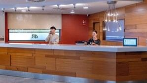 Balcão de recepção de hotel com design moderno, destacando um painel de parede de madeira e uma tela digital.